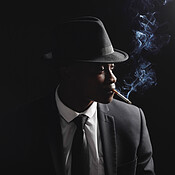 African man wearing a formal suit and hat while smoking against a black ...
