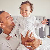 A happy dad and baby with smile on the bed at home, having fun and ...