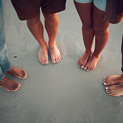 Friends, feet and beach in water, sand and travel summer vacation with ...