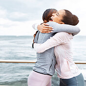 Fitness, friends and women hug at the ocean, success and workout goals ...