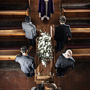 Funeral, church and sad people carrying coffin with a priest ...