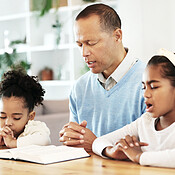 Family, worship and bible with father and kids praying at table for ...