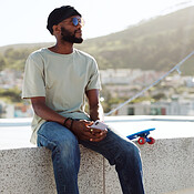 Black man, relax and rest on wall with skateboard on building rooftop ...