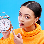 Woman, annoyed and point at alarm clock in portrait for warning by blue ...
