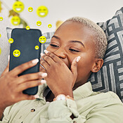 Black woman on sofa with phone, laughing and emoji on social media ...
