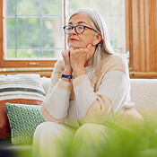 Thinking, reflection and senior woman on sofa in the living room with memory or dreaming face ...