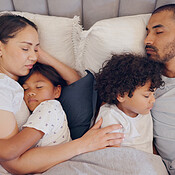 Tired, sleeping and parents with children in bed on a weekend morning ...