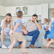Stressed parents sitting on couch with children running around.Excited ...