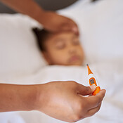Sick little girl in bed while her mother uses a thermometer to check her temperature. Mixed race ...