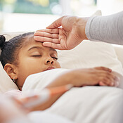 Sick little girl in bed while concerned mother uses a thermometer to check her temperature ...