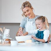 Happy mother helping her daughter bake. Parent baking with her child. Young woman helping her ...
