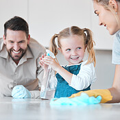 Happy family cleaning the kitchen together. Little girl spraying ...