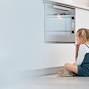 Little girl patiently waiting by the oven. Caucasian child sitting and ...