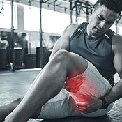 Young athlete in pain in the gym. Fit bodybuilder sitting on the floor ...