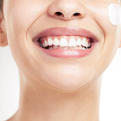 Face of a beautiful woman showing her smile and teeth applying cream on ...