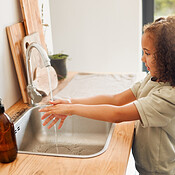 One mixed race adorable little girl washing her hands in a kitchen sink ...