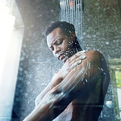 Black man, shower and foam in bathroom, home or washing body for hygiene with low angle in ...