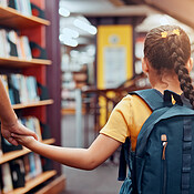 Education, tutor and child in library, bookshelf and holding hands with ...
