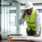 A male engineer talking on the phone, smiling and standing in an office ...