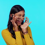 Face, sunglasses and woman wink in studio isolated on a blue background ...