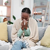 Sneeze, blowing nose and black woman on a sofa with tissue, flu or ...