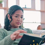 Woman, reading book and cringe or disgust on couch with facial ...