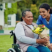 Gift, wheelchair and caregiver with flowers for senior woman in a ...